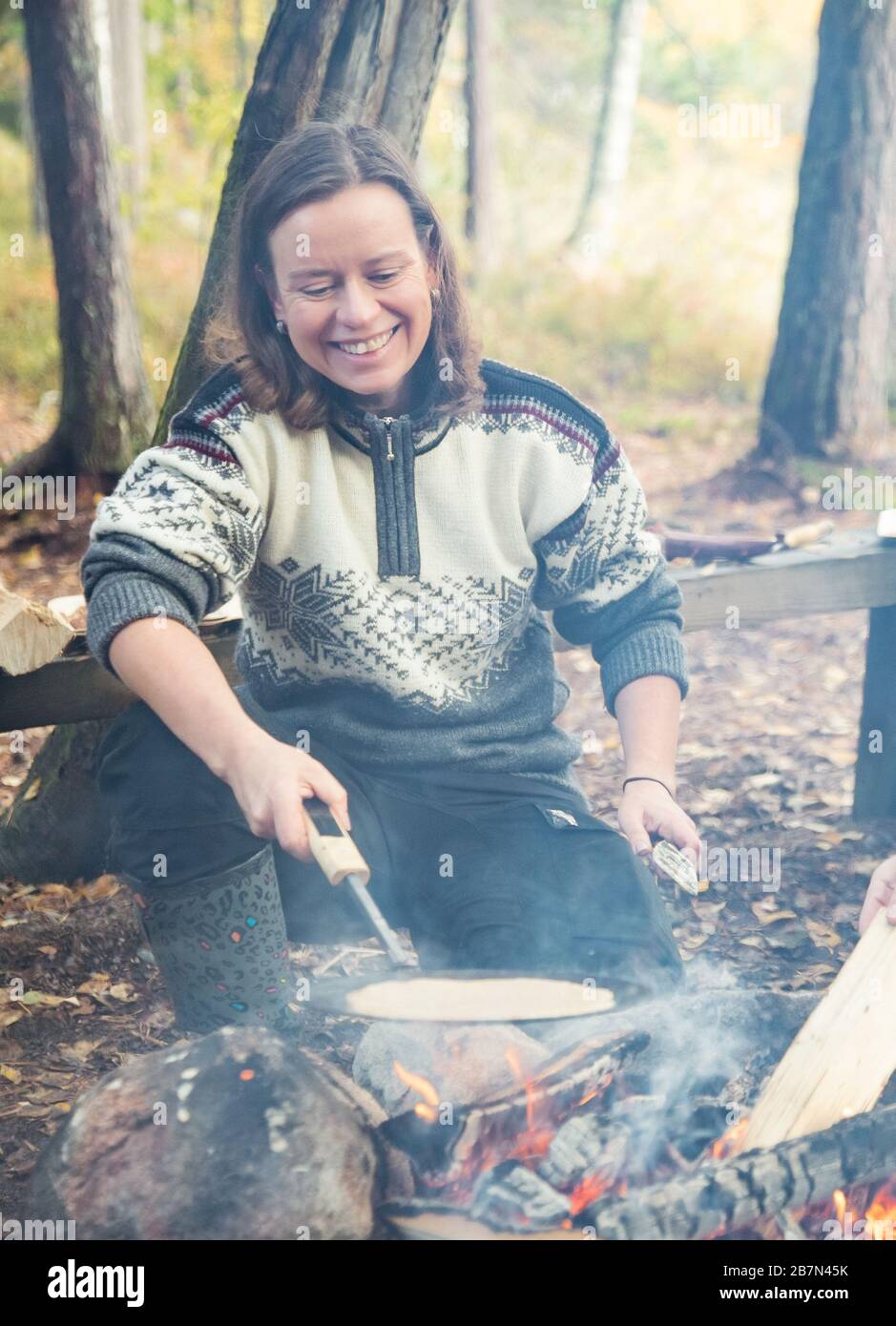 Man and woman making pancakes on campfire in forest on shore of lake ...