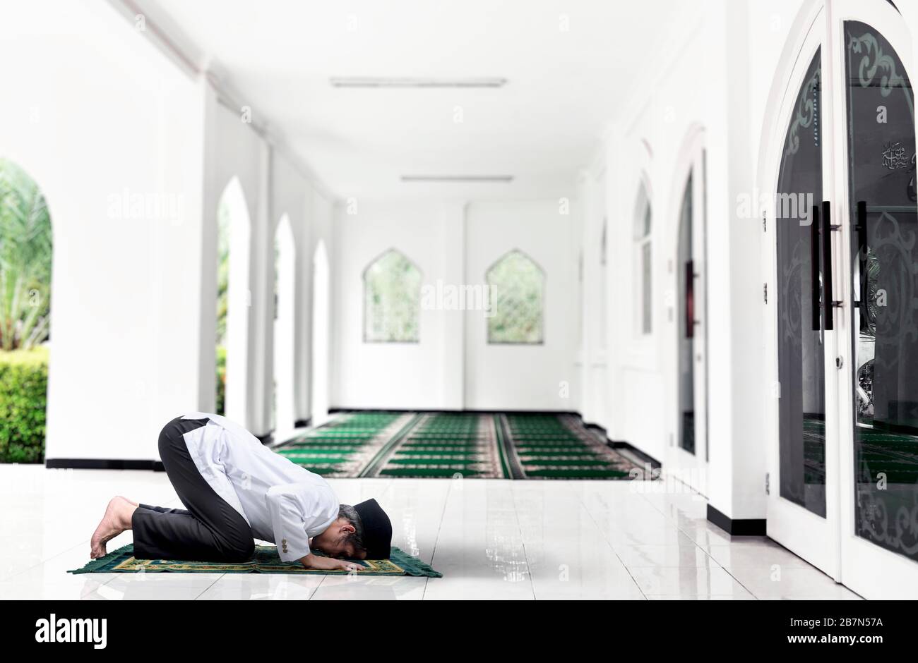 Asian Muslim man with a prayer rug in a praying position (salat) inside ...
