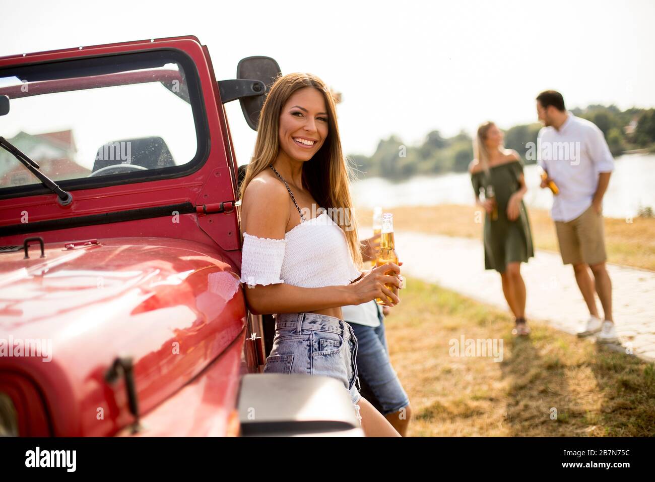 Happy young women drinks cider from the bottle by the convertible car ...