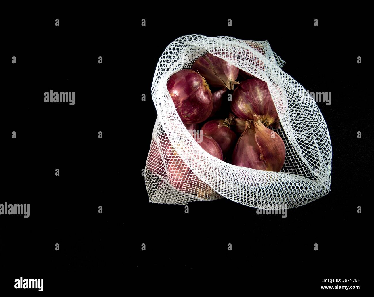 Red onions in mesh bag and some on floor isolated on black background ...