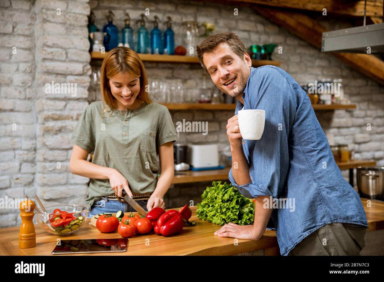 Young woman cooking while man drinking coffee in the rustic kitchen ...