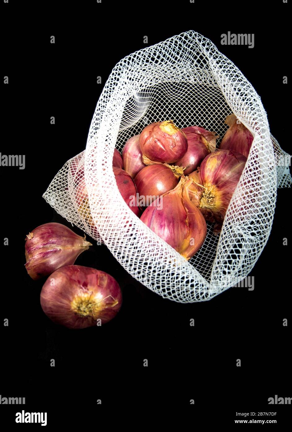 Red onions in mesh bag and some on floor isolated on black background ...