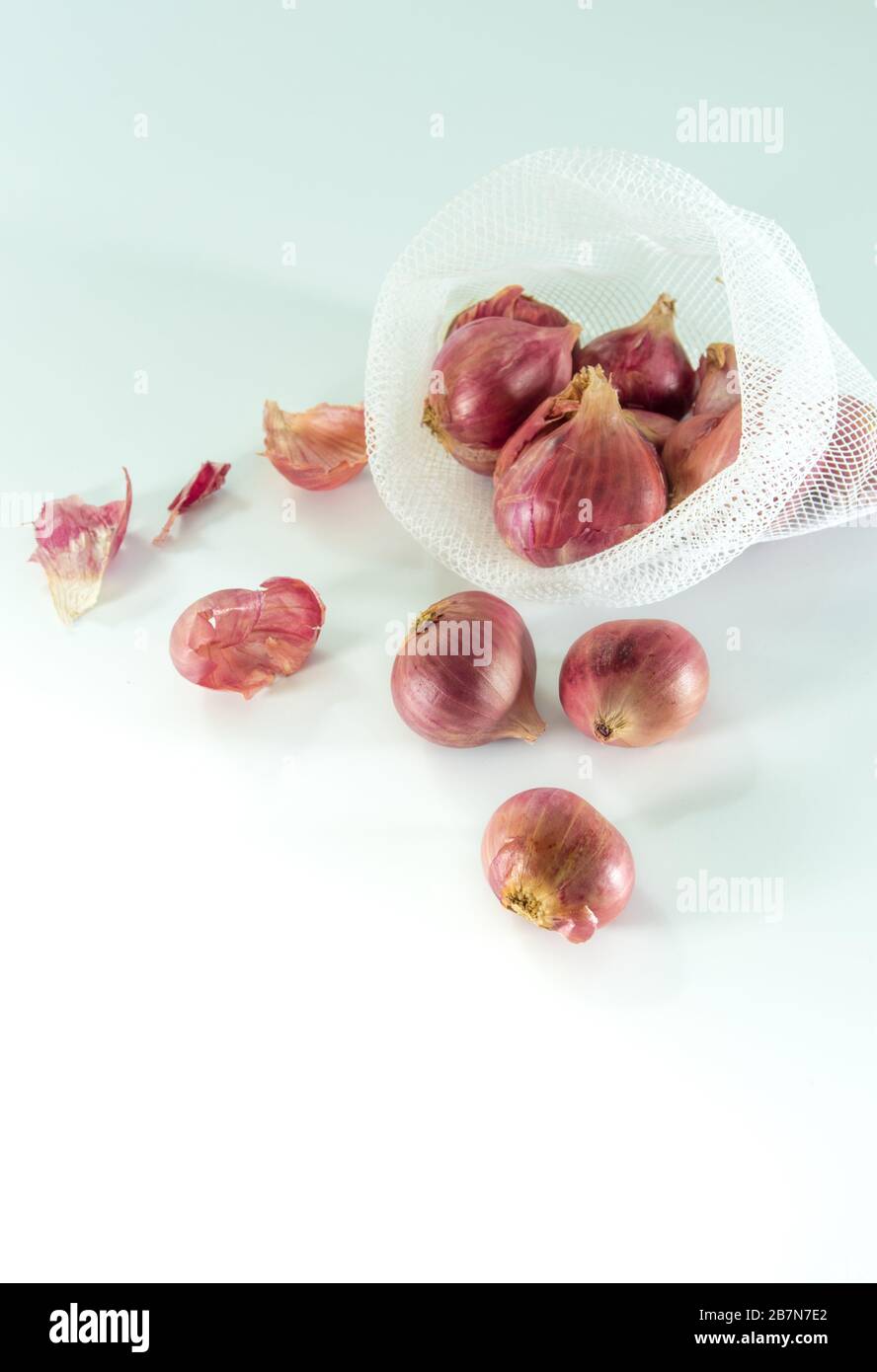 Red onions in mesh bag and some on floor isolated on white background ...