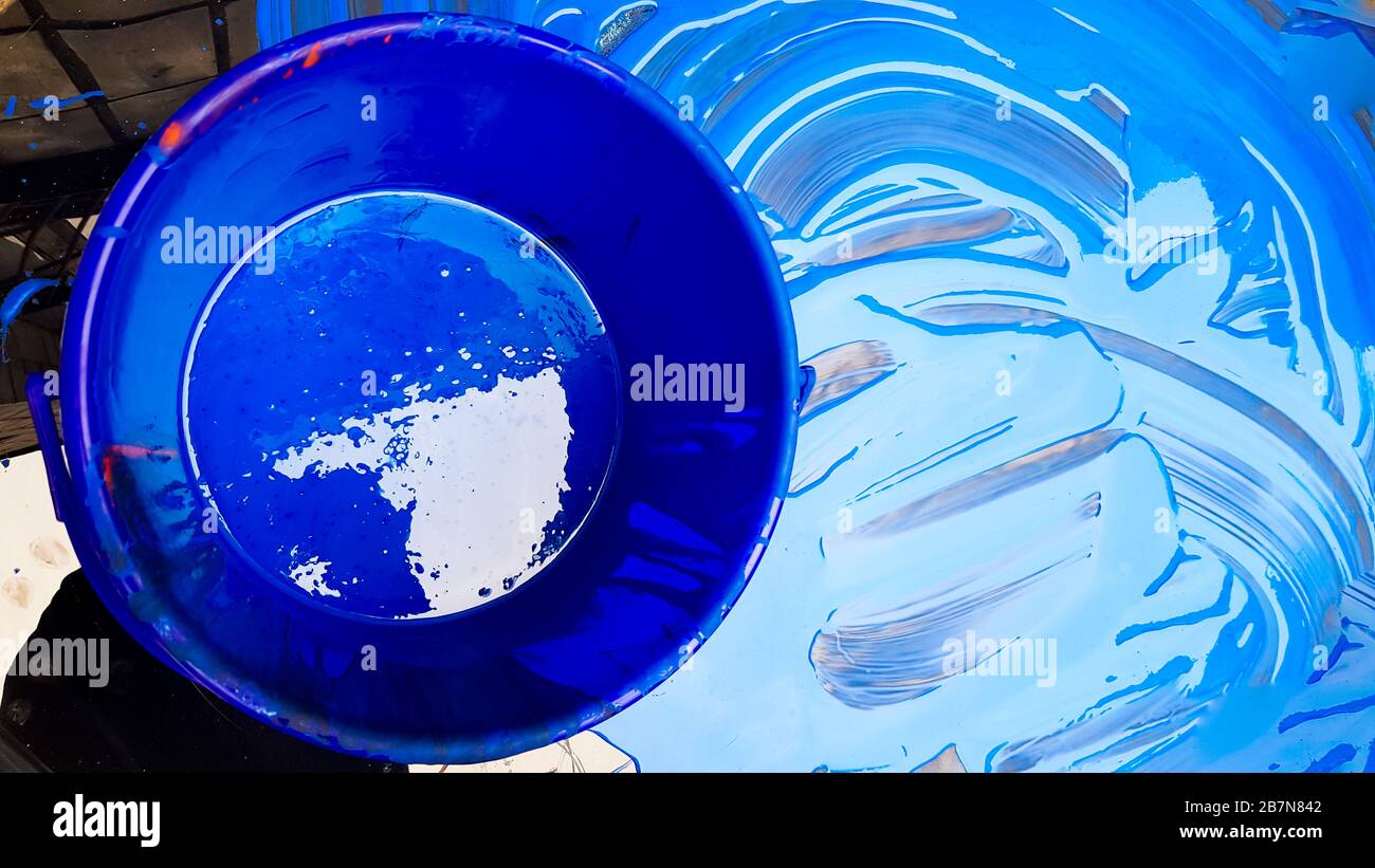 Abstract background of spilled blue paint with buckets on a black ...