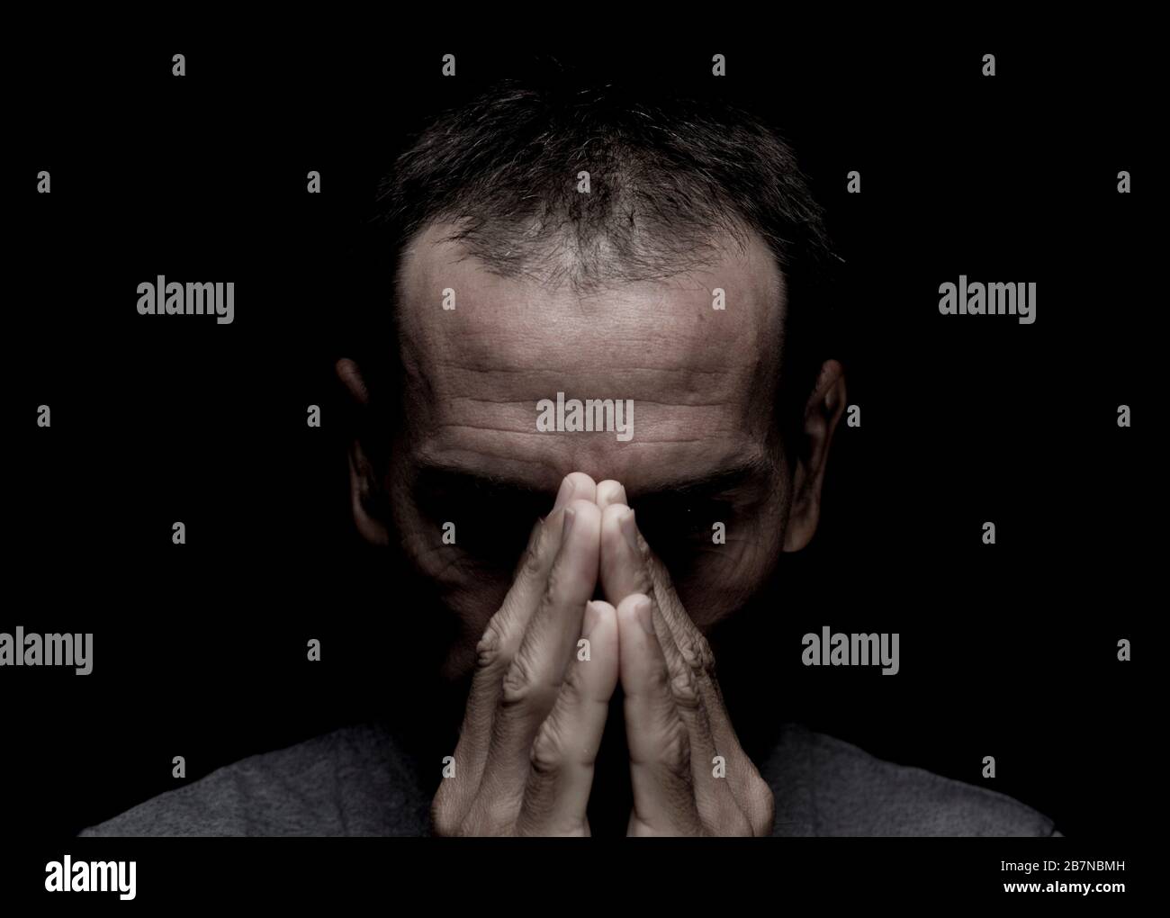 worried man crestfallen praying in black background desaturated Stock ...
