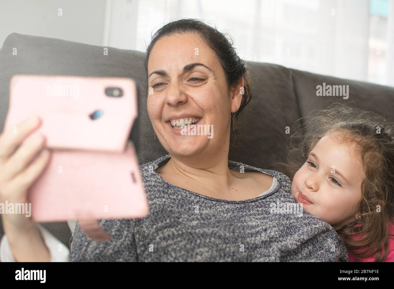 Young mother and daughter smiling while videoconferencing at home ... Young mother and daughter smiling while videoconferencing at home ...