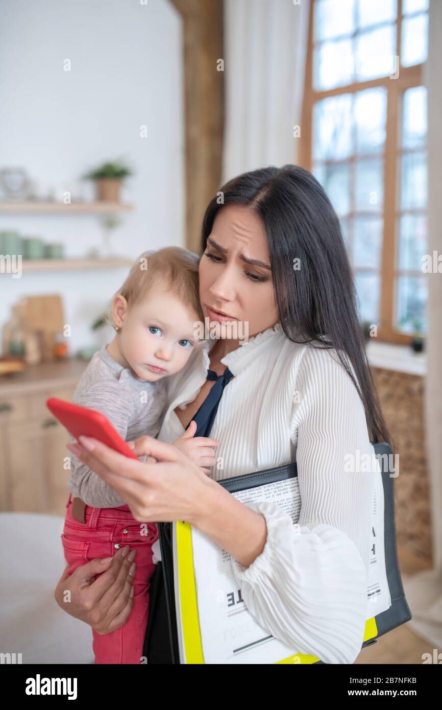 Working mom checking phone, holding her baby Stock Photo - Alamy