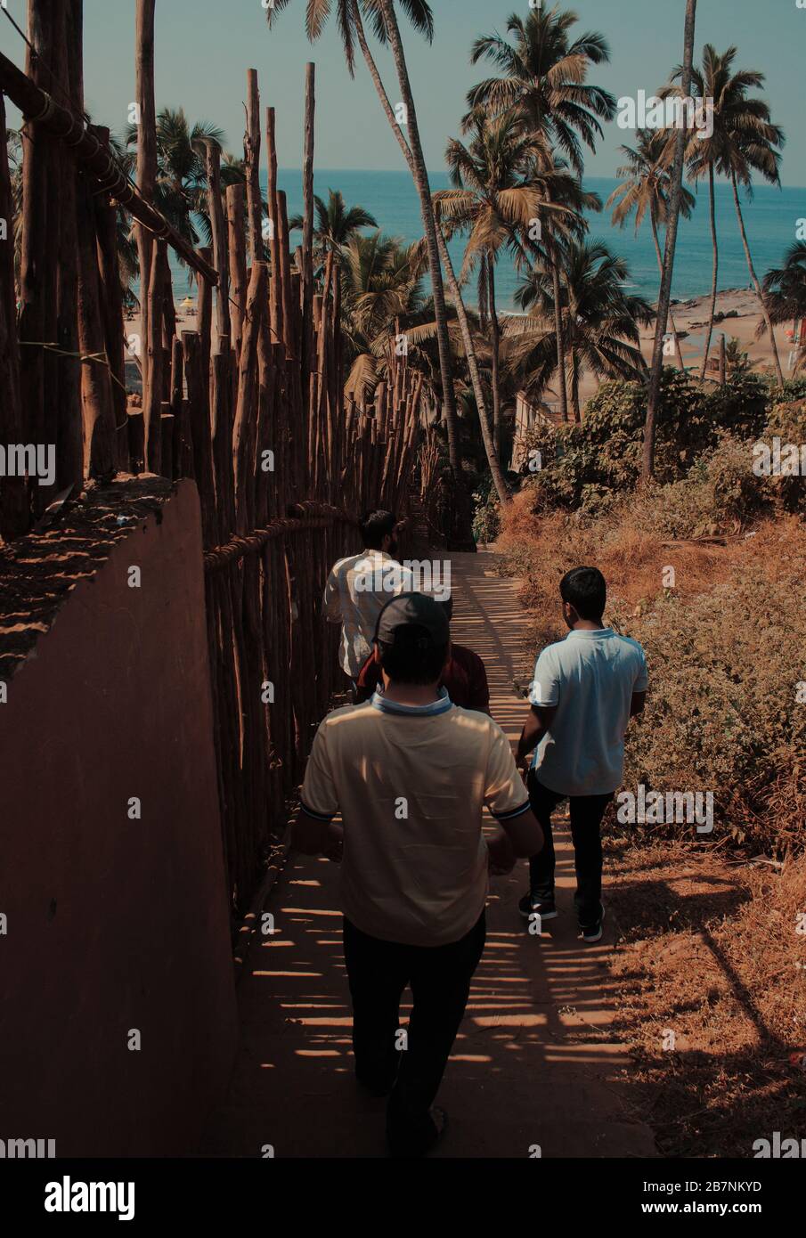 Group of men walking on a path lined with wooden fence in a village ...