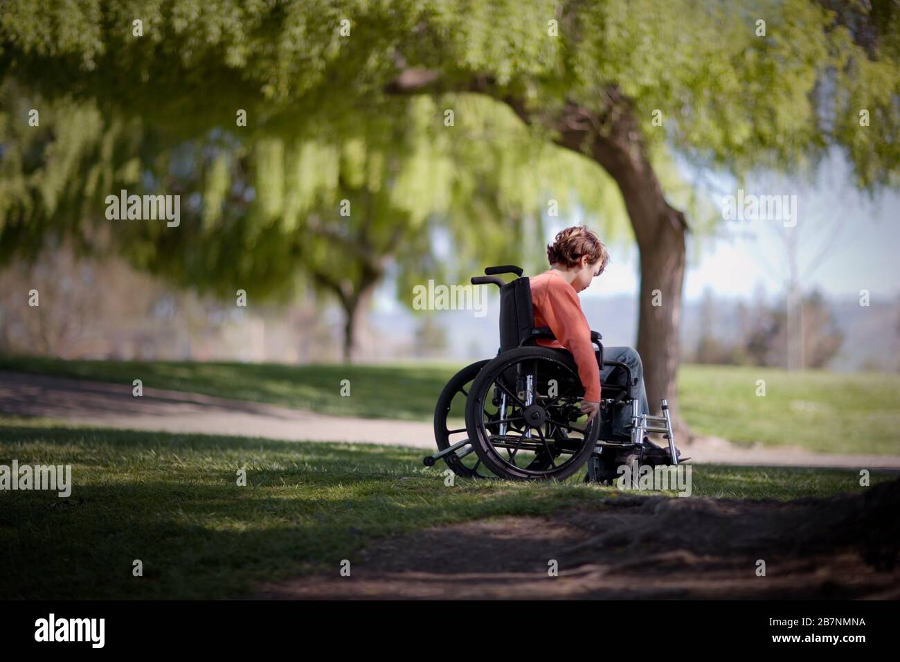 Young boy wheeling himself in a wheelchair at the park Stock Photo - Alamy