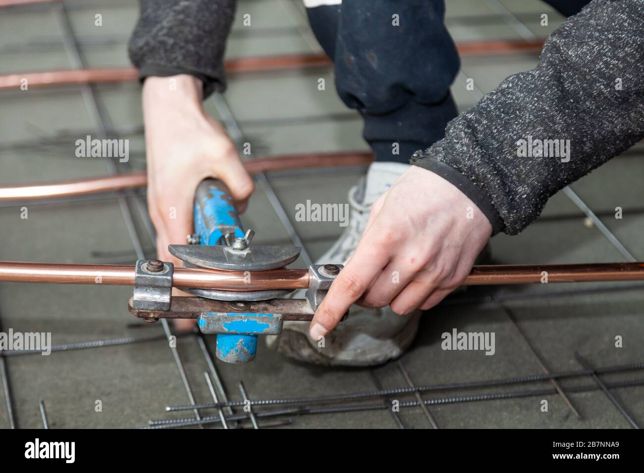 Close-up male worker's hands bends new copper pipes by blue pipe bender ...