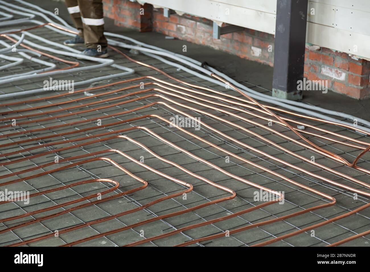 Close-up bent new shiny copper pipes with plastic braid on floor, lay ...