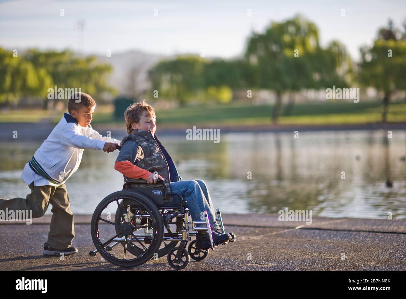 Boy pushing friend in wheelchair through park Stock Photo - Alamy