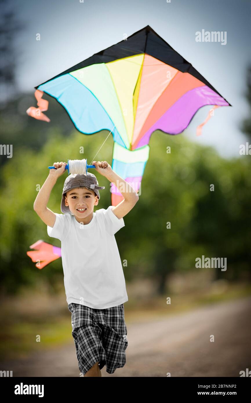 Portrait of a young boy running while flying a kite behind him outdoors ...