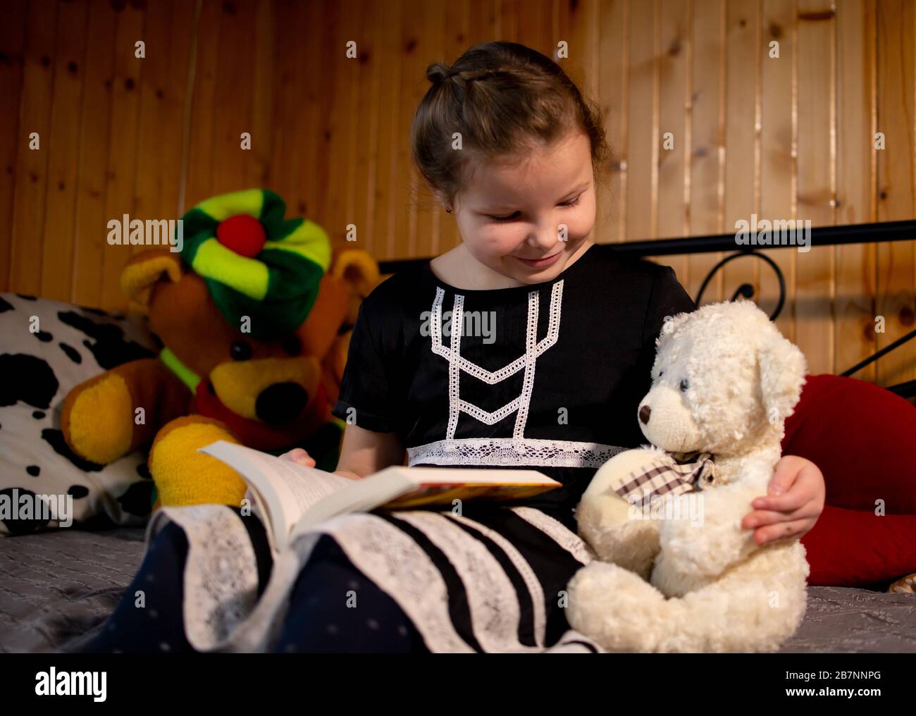 little girl with her teddy bear reading a book on the sofa at home ...