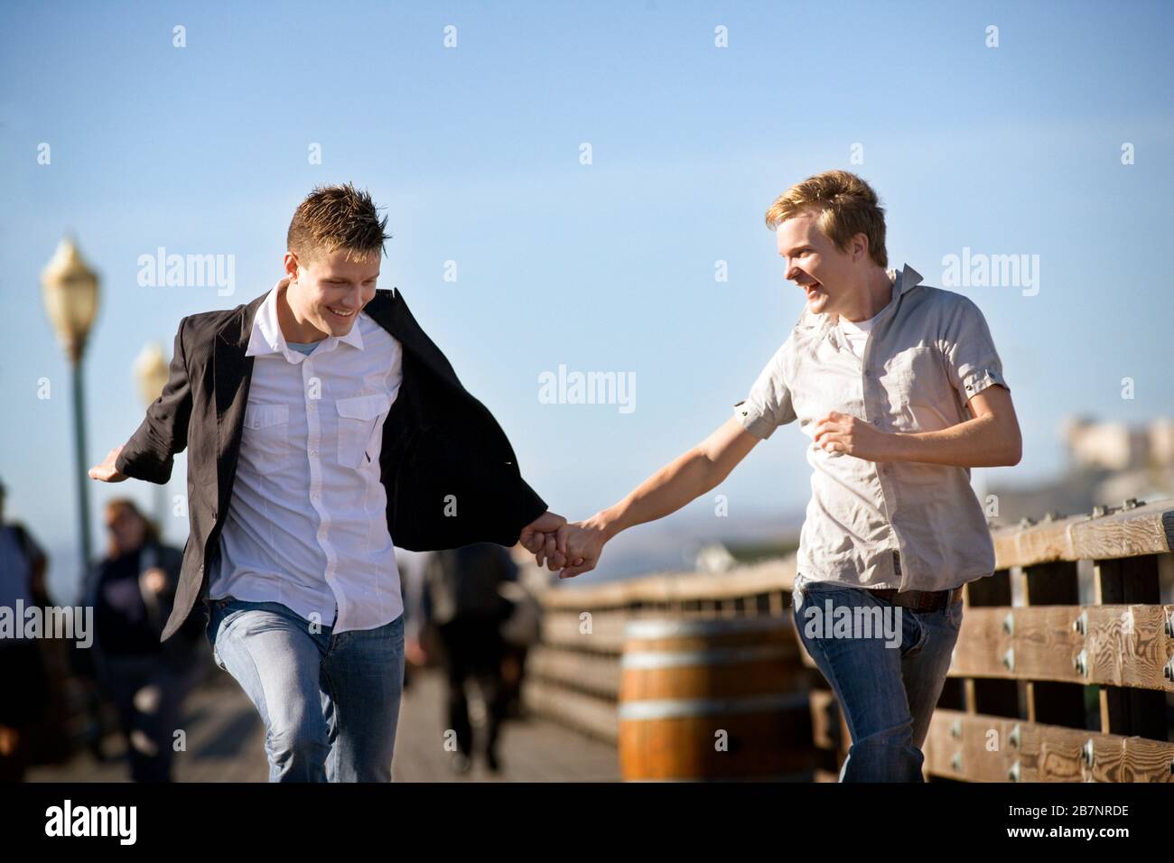 Two smiling young homosexual men running together while holding hands ...
