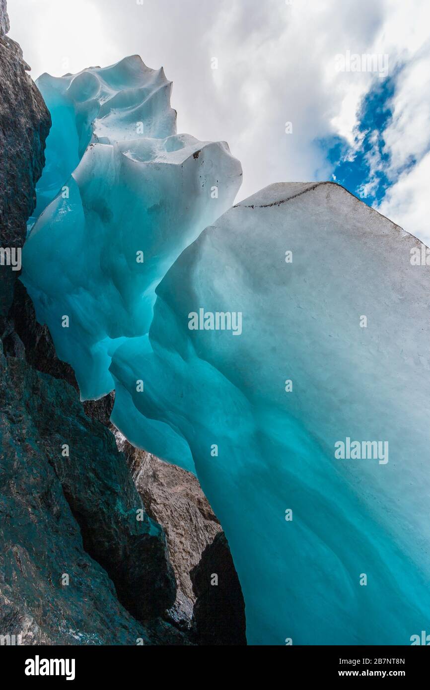 Beautiful ice of blue color hanging from stones. A small stream of ...