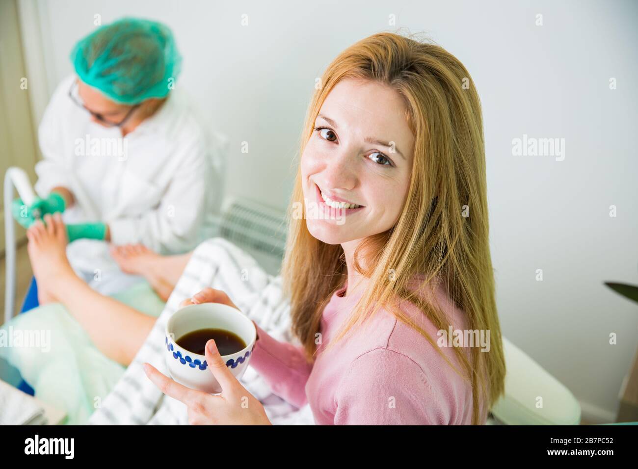 Woman relaxing in chair with cup of coffee, having foot treatment in ...
