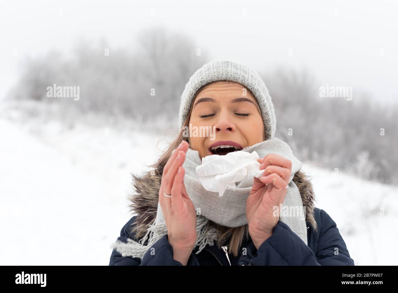 Portrait of a young woman sneezing , holding a tissue outdoor in ...