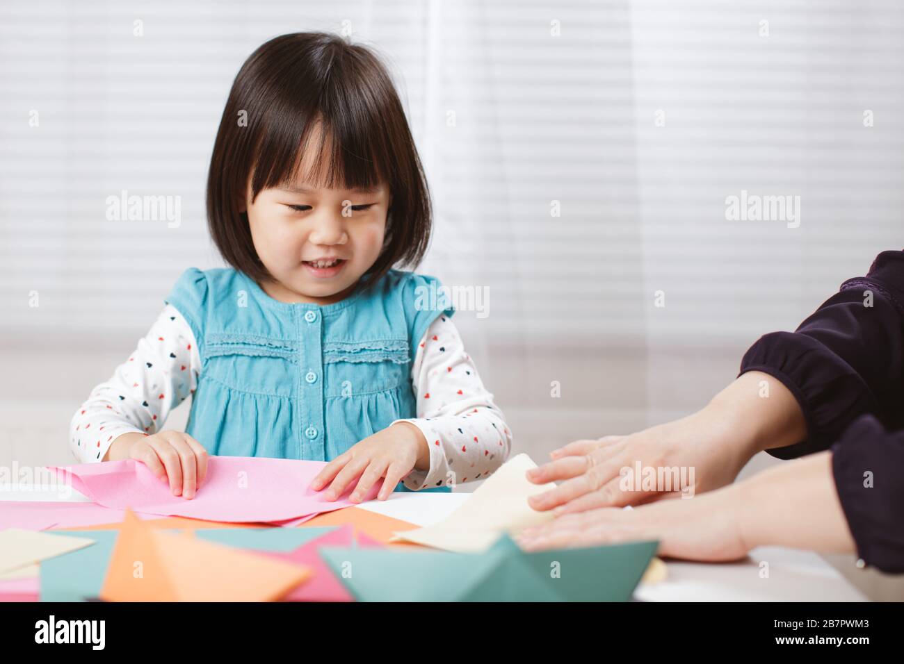 toddler girl learn making Origami at home against white background ...