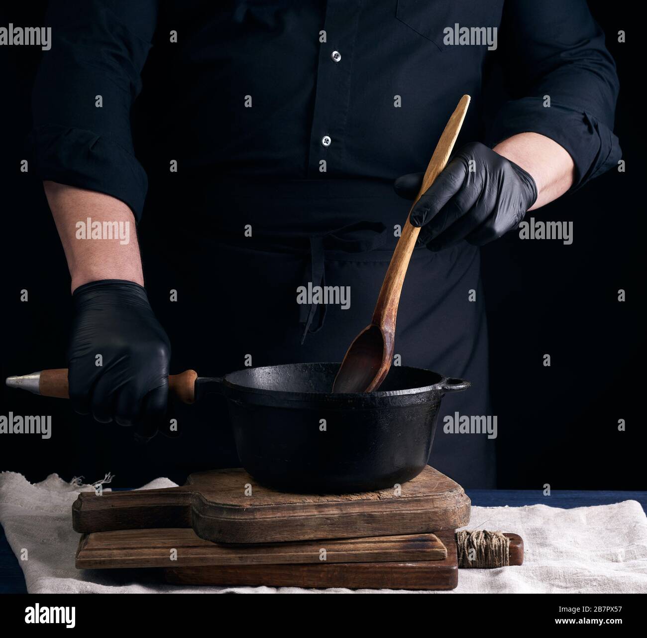 male cook in black uniform and latex gloves stirs a vintage wooden ...