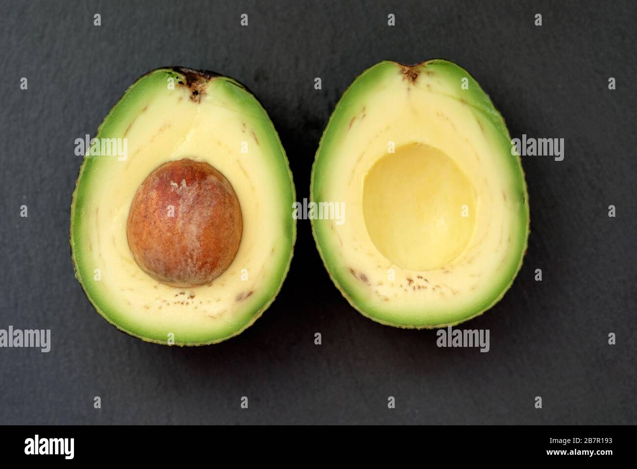 Two halves of avocado on a black background top view. Green sliced ...