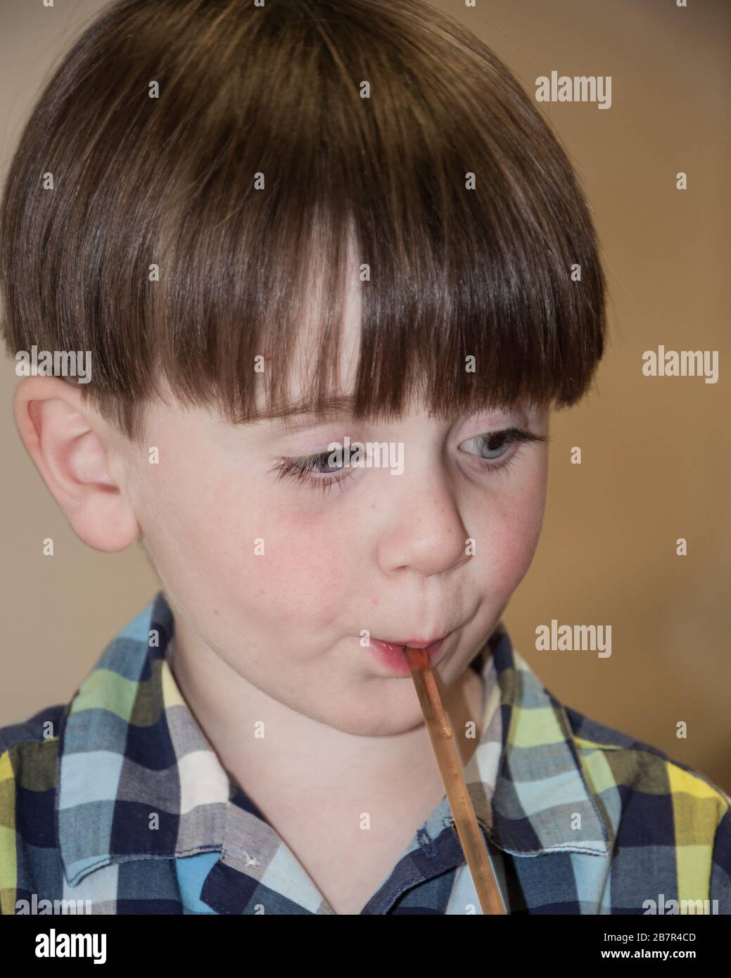 Young boy with blue eyes sipping a soft drink from a straw looking ...