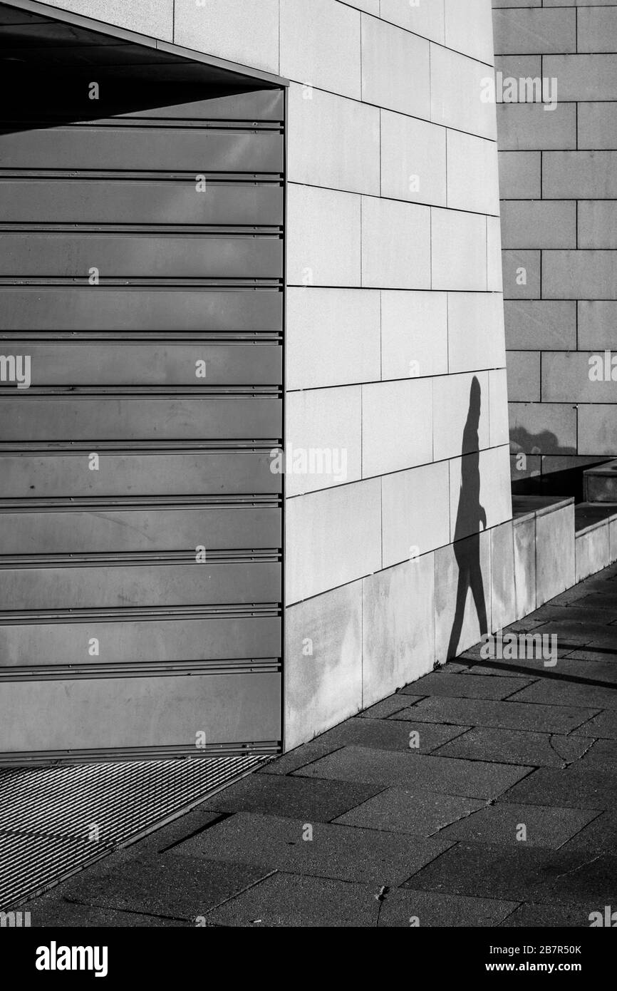 Shadow of a man walking along a building with strict lines and angles ...