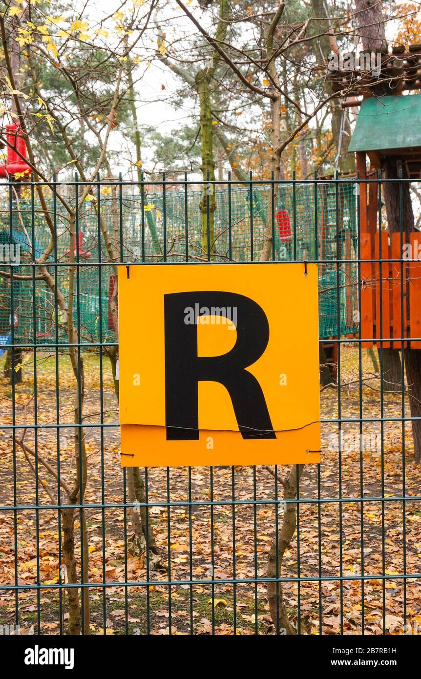 Vertical shot of an orange sign with the letter R on a metal fence ...