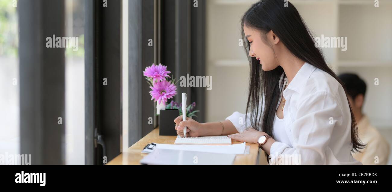 Side view of young female college student take short note while reading ...