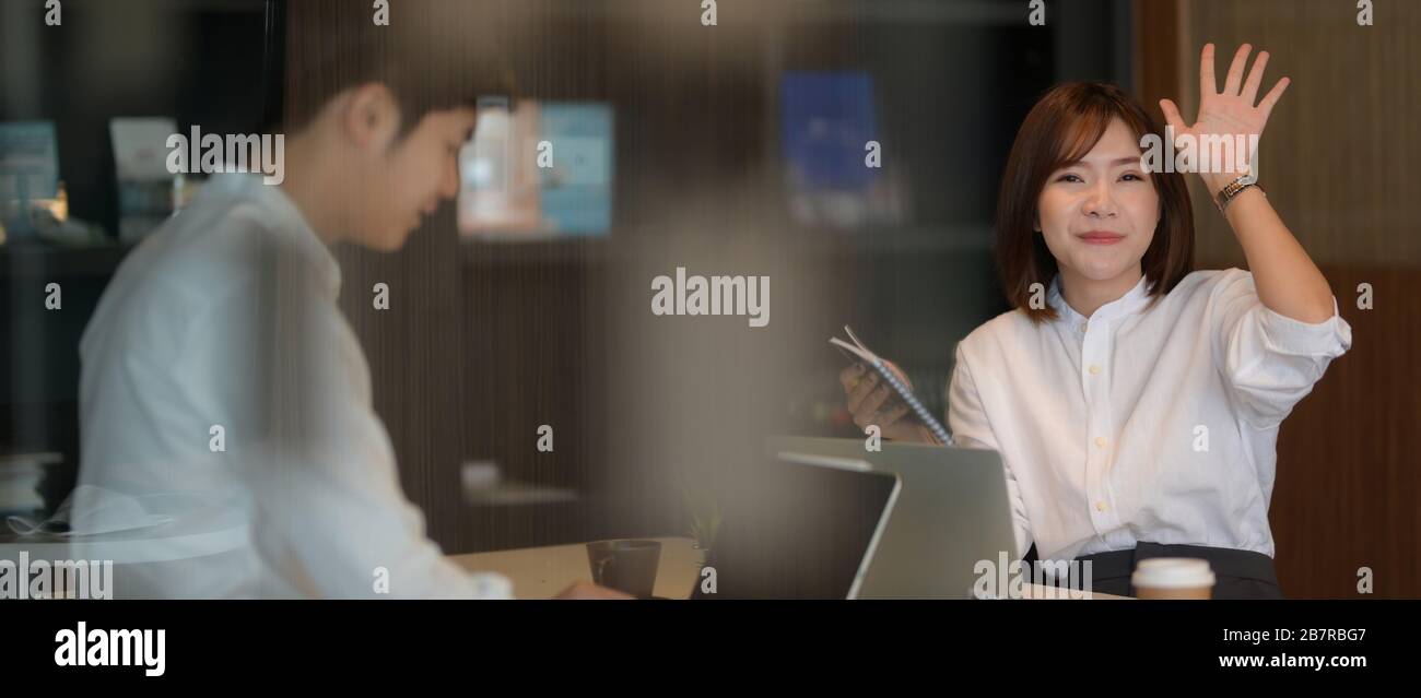 View through glass window of young businesswoman greeting her colleague ...