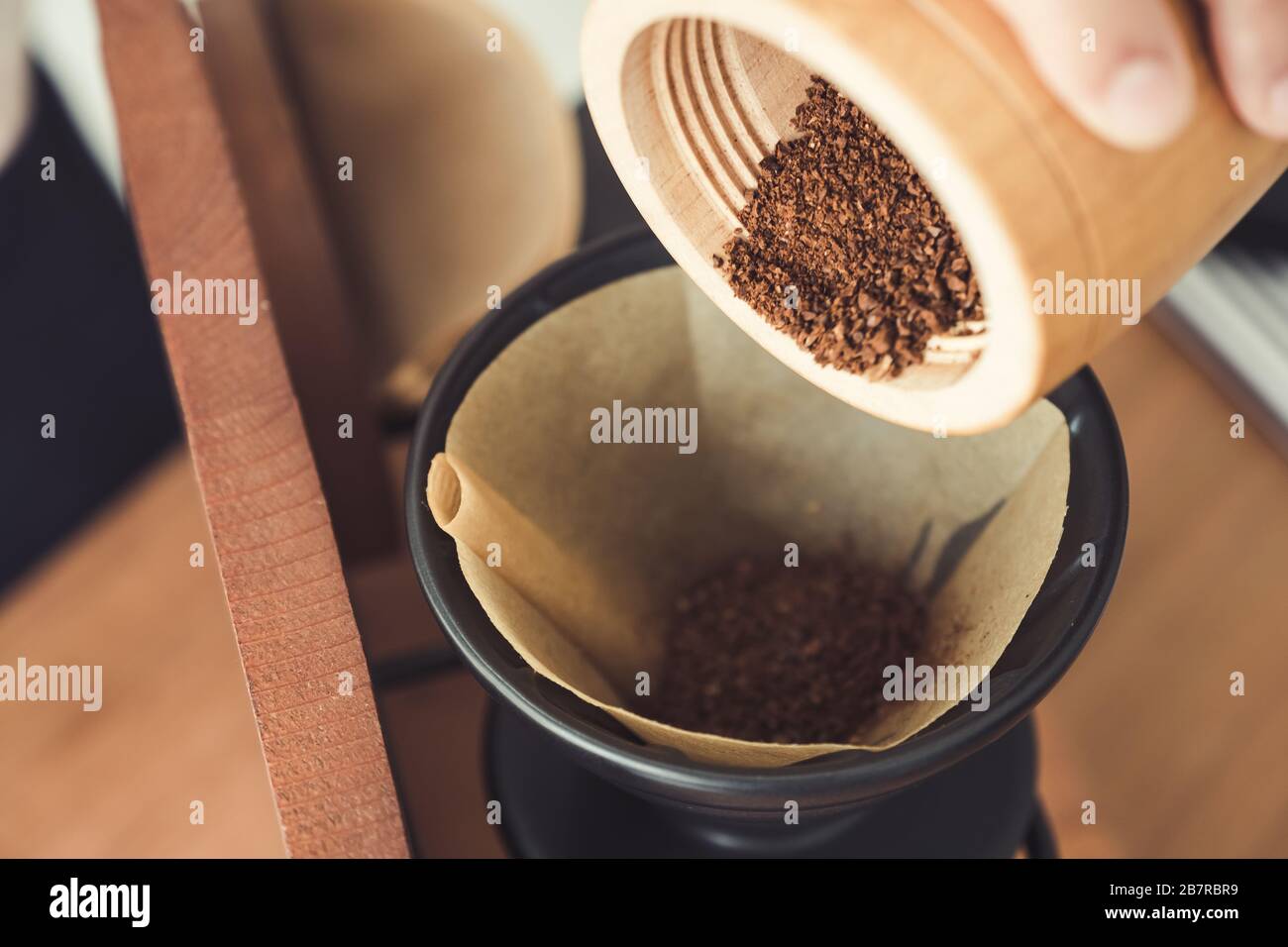 Closeup image of a hand pouring coffee from wooden grinder into a drip ...