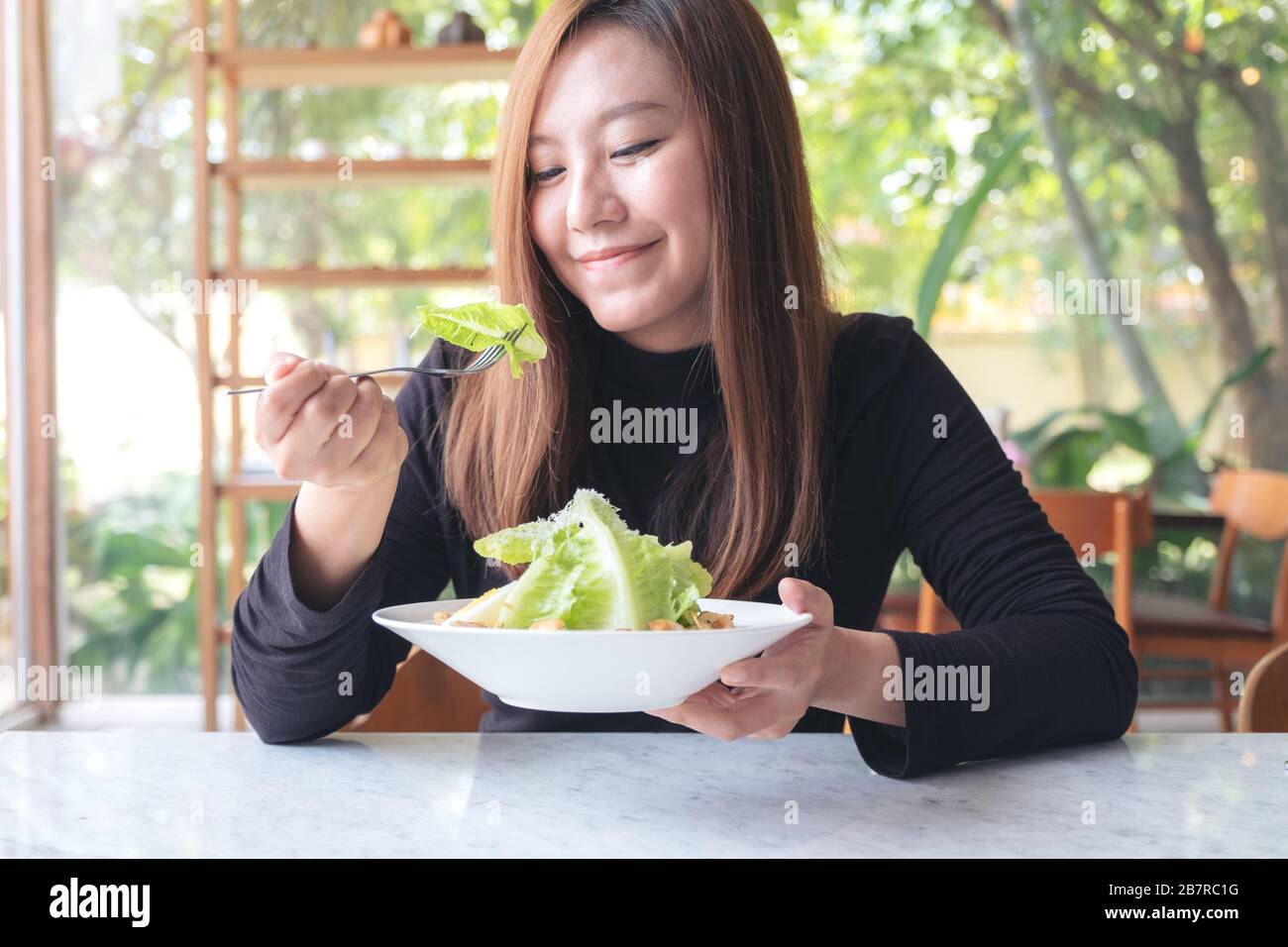 A beautiful asian woman enjoy eating caesar salad on table in the ...