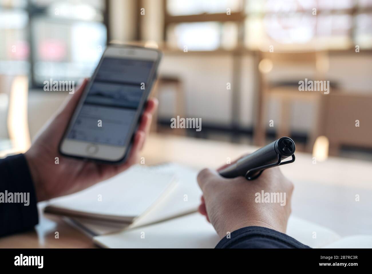 Closeup image of hands holding a smart phone and a pen to write Stock ...