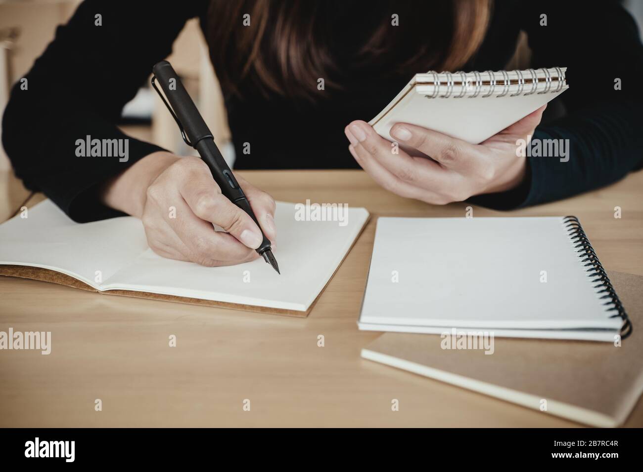 A woman holding and writing on notebook while sitting in cafe with blur ...