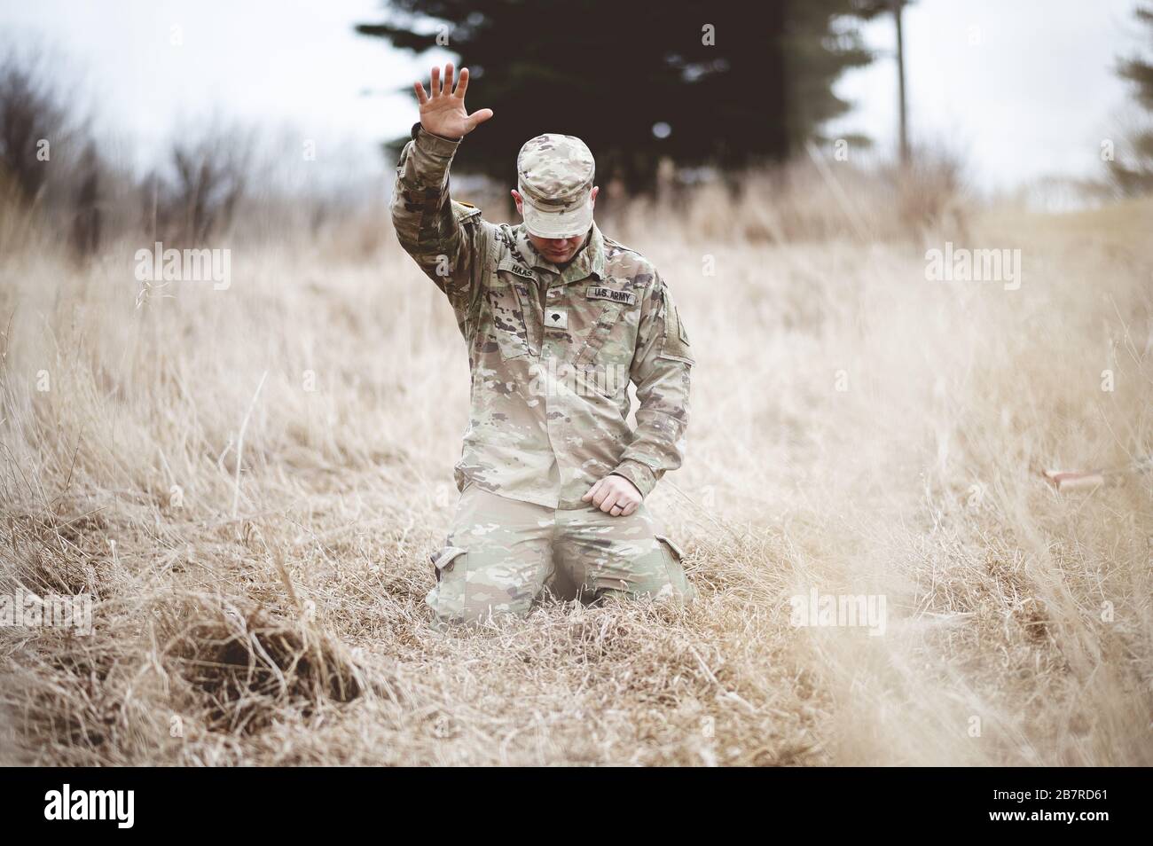American soldier kneeling in despair on a grass field with his hand ...