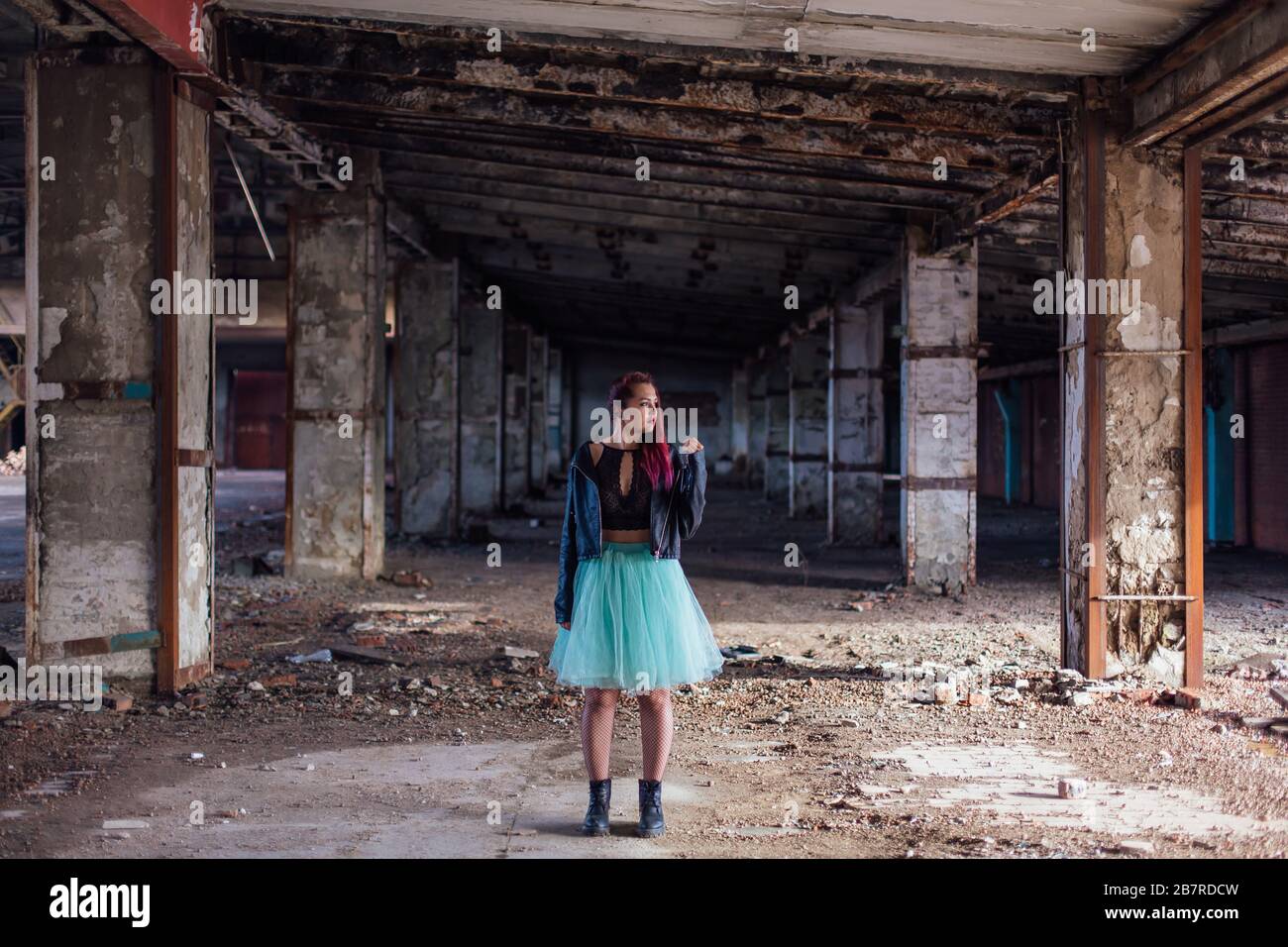 Portrait of a young girl with pink hair standing inside of collapsed ...