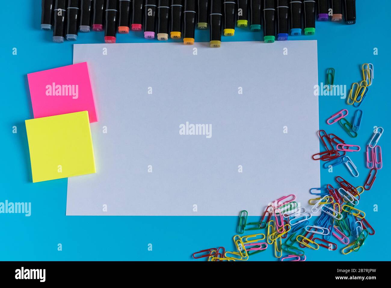 Multi-colored markers, paper clips, stickers and paper on a blue ...