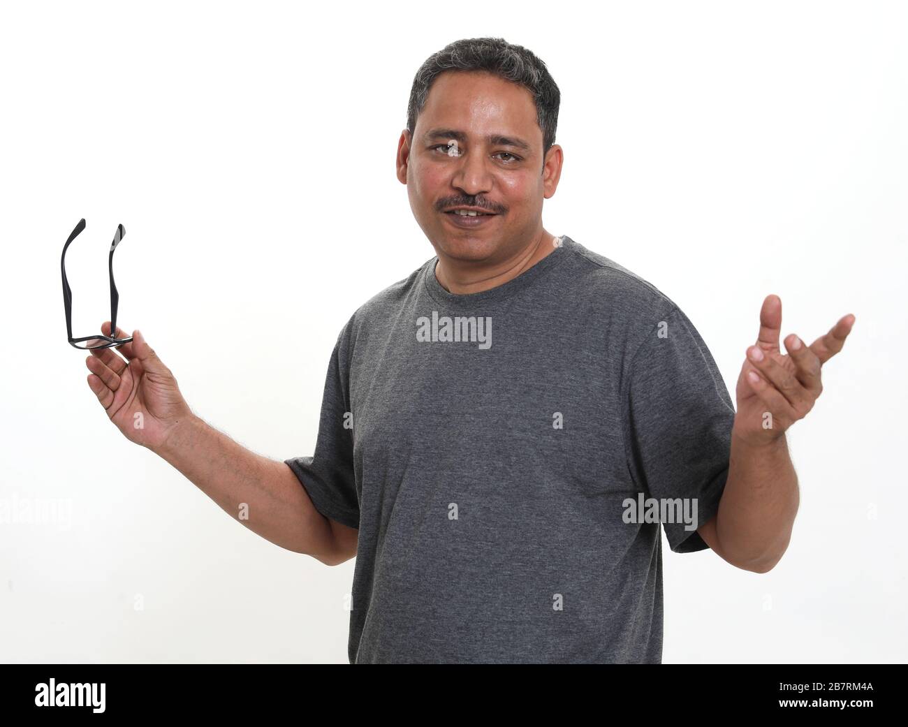 A smiling Indian man holding spectacles in a studio against a white ...