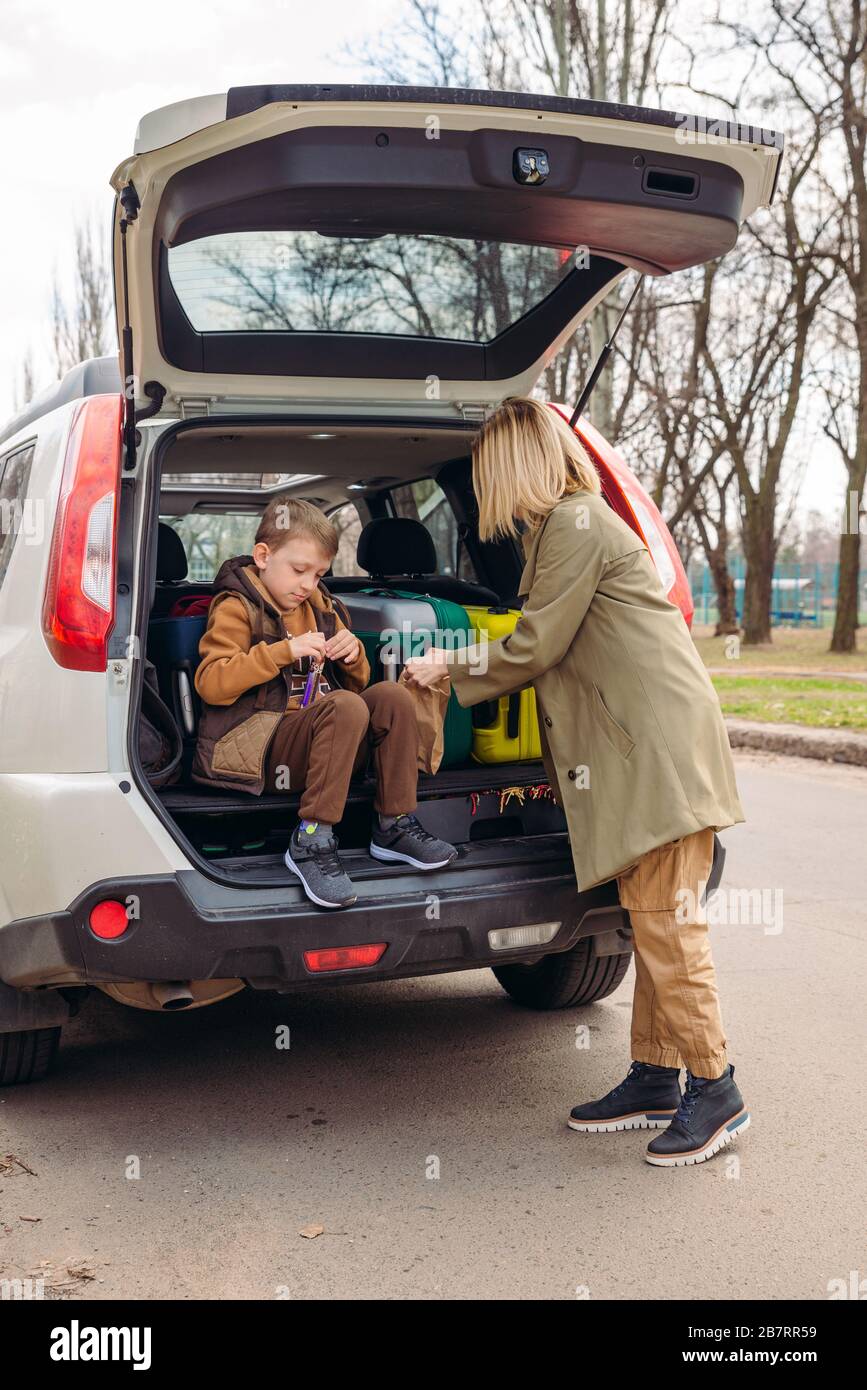 little kid sitting with mother in car trunk full of luggage eating ...