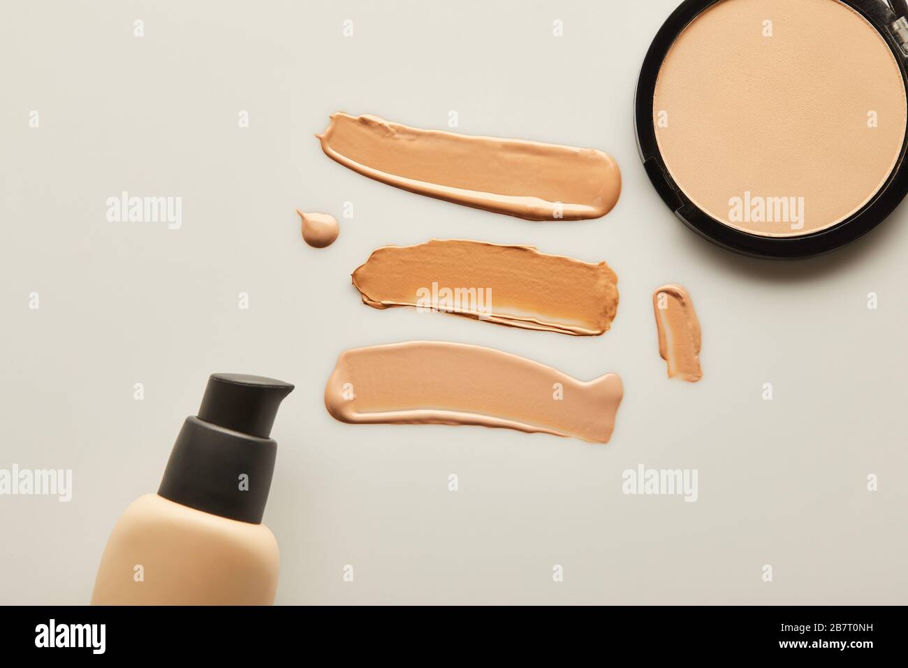 Top view of dispenser, tone cream brushstrokes with face powder on grey ...