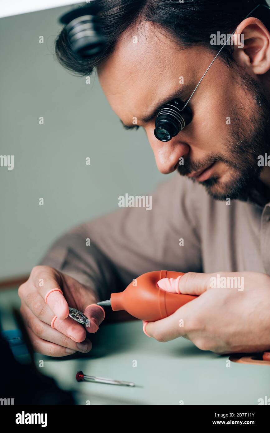 Side view of watchmaker in eyeglass loupe working with watch part and ...