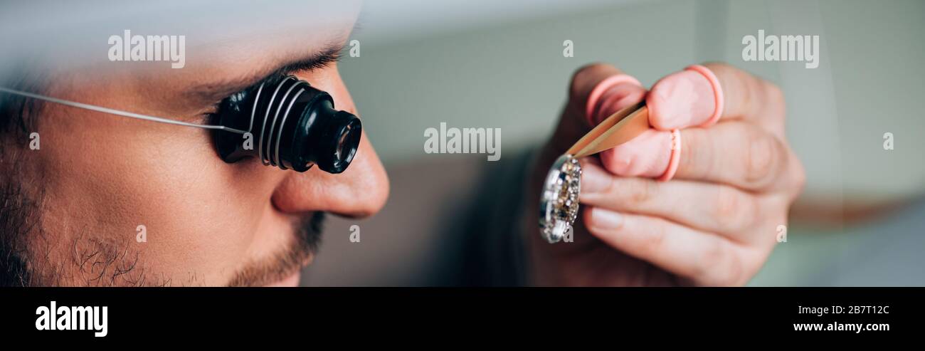 Panoramic shot of watchmaker in eyeglass loupe holding watch detail in ...