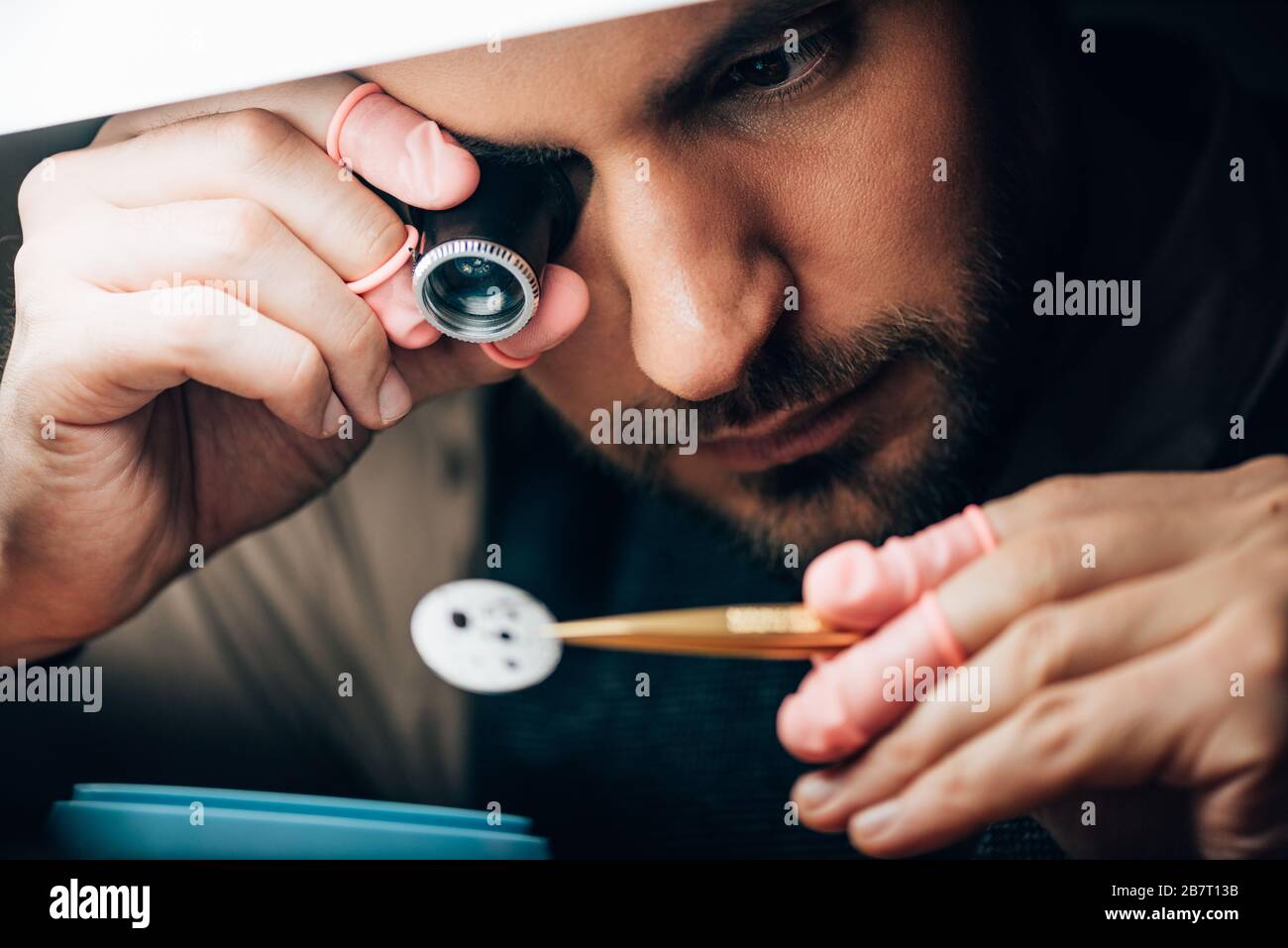 Selective focus of watchmaker holding eyeglass loupe and watch part by ...