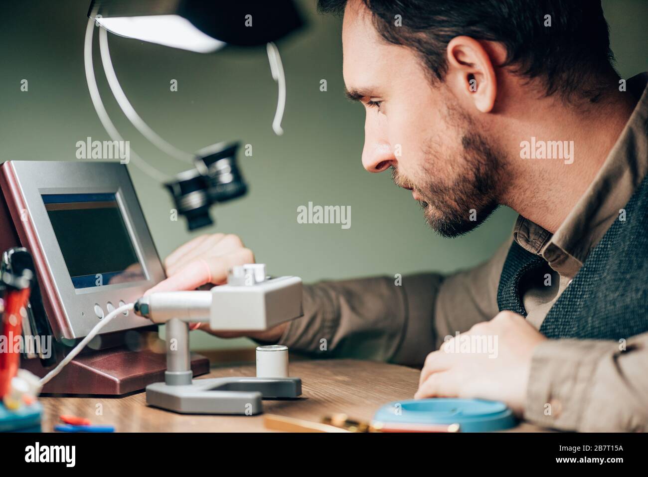 Side view of watchmaker using timegrapher while working at table Stock ...