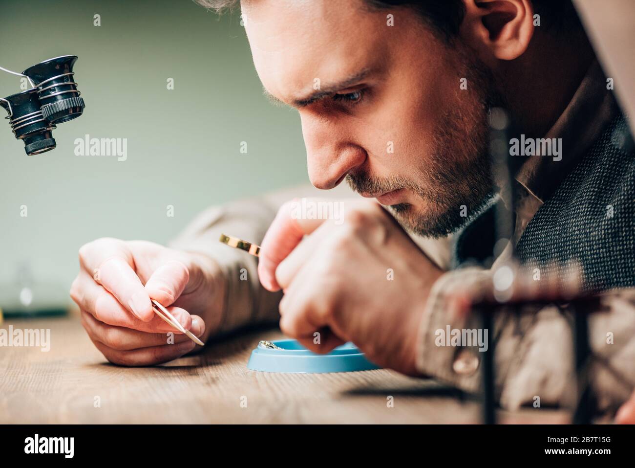 Side view of handsome watchmaker using magnifying glass for clock part ...