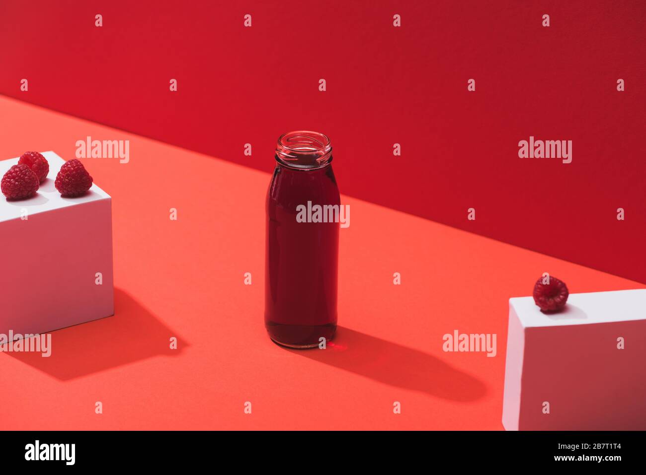 fresh berry juice in glass bottle near ripe raspberries on cubes on red ...