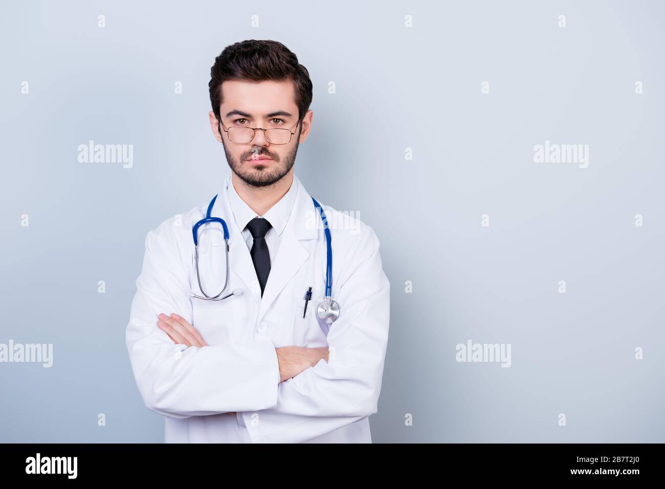Portrait of concentrated minded doctor in white coat standing with ...