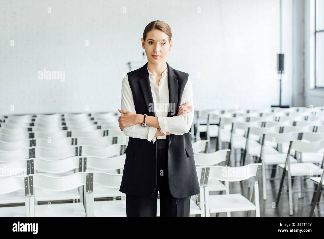 attractive woman in formal wear with crossed arms in conference hall ...