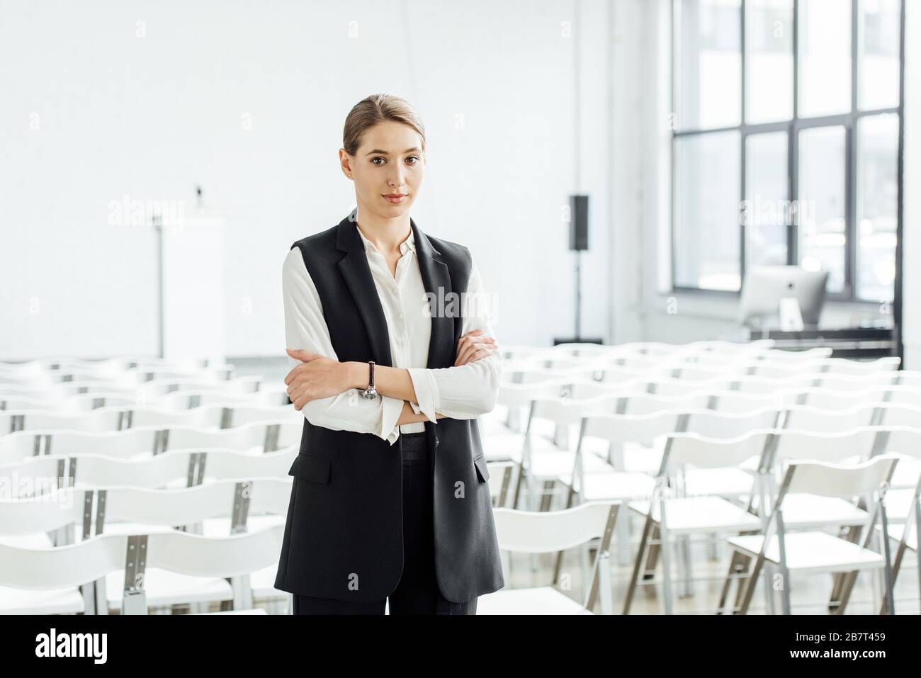 attractive woman in formal wear with crossed arms in conference hall ...