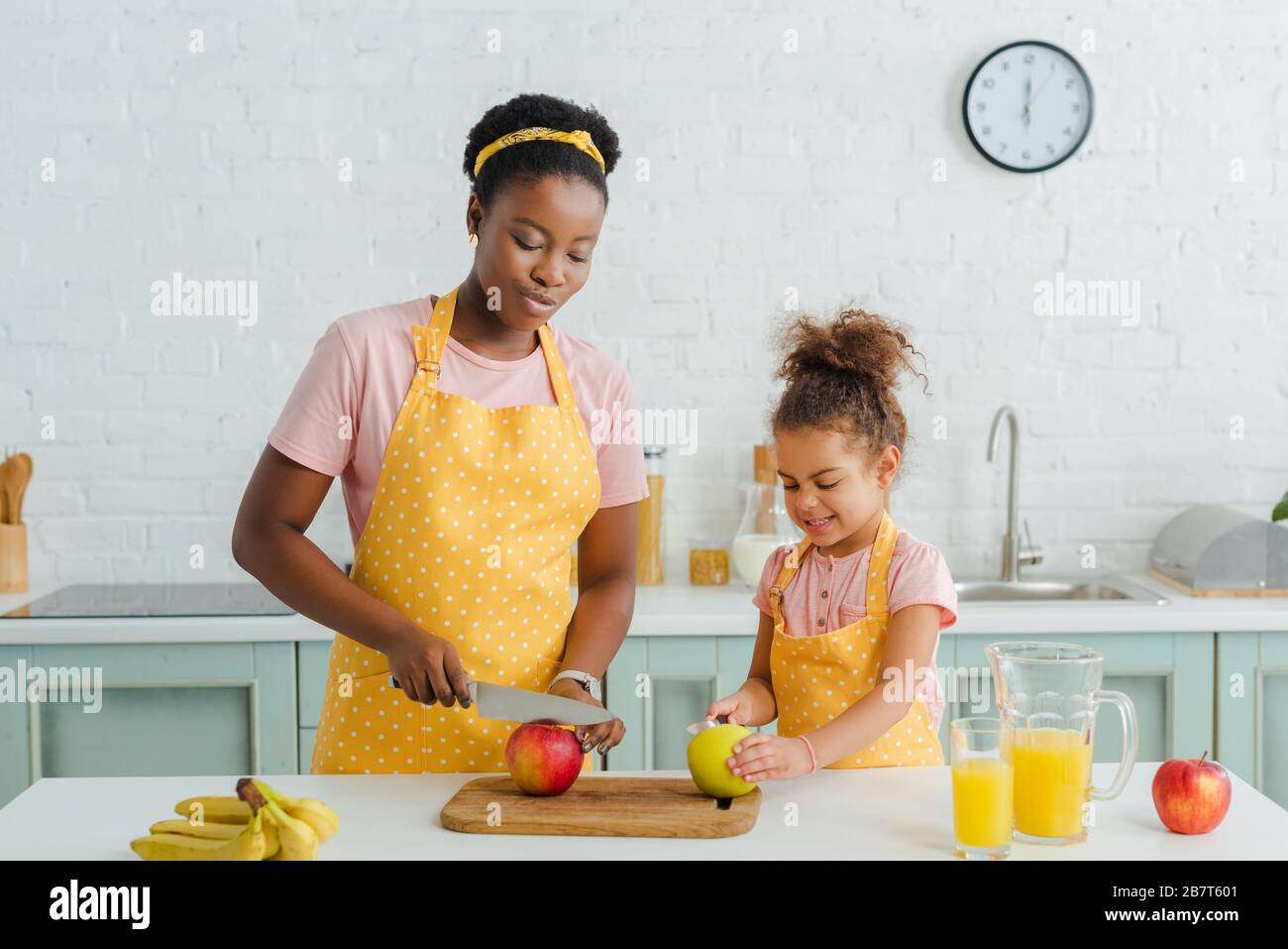 attractive african american mother cutting apple near cute daughter ...
